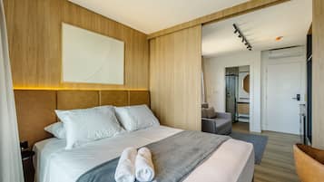 Quarto de hotel moderno com cama grande, cabeceira, mesa de cabeceira e vista para o quarto vizinho.