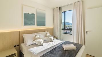 Quarto de hotel com uma cama, mesa de cabeceira, janela com cortinas e obra de arte na parede.