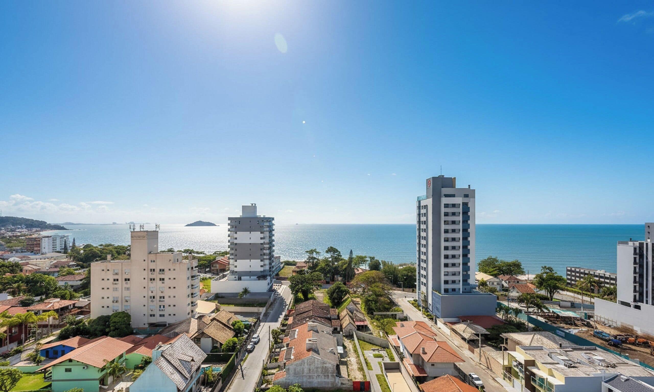 Paisagem costeira urbana com edifícios modernos, céu claro e vista para o mar.