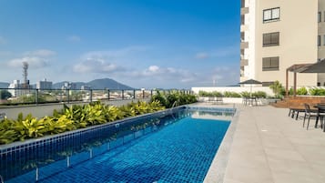 Piscina no terraço com piso de azulejos, rodeada por vegetação e mobiliário para áreas externas.