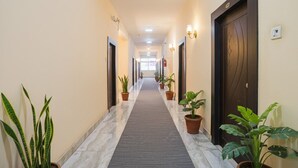 Corredor de hotel com piso de mármore, plantas em vasos e portas em ambos os lados.