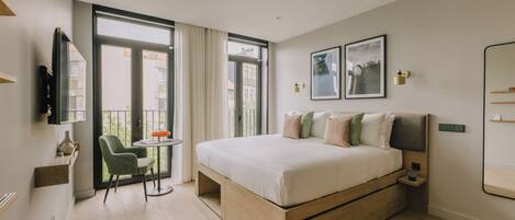 Quarto de hotel moderno com uma cama grande, uma mesa pequena, uma cadeira, uma televisão e uma varanda com cortinas.