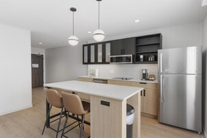 Uma cozinha moderna com ilha central, eletrodomésticos de aço inoxidável e iluminação pendente.