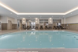 Uma grande piscina interior com água cristalina, rodeada por espreguiçadeiras e um chão em mosaico.