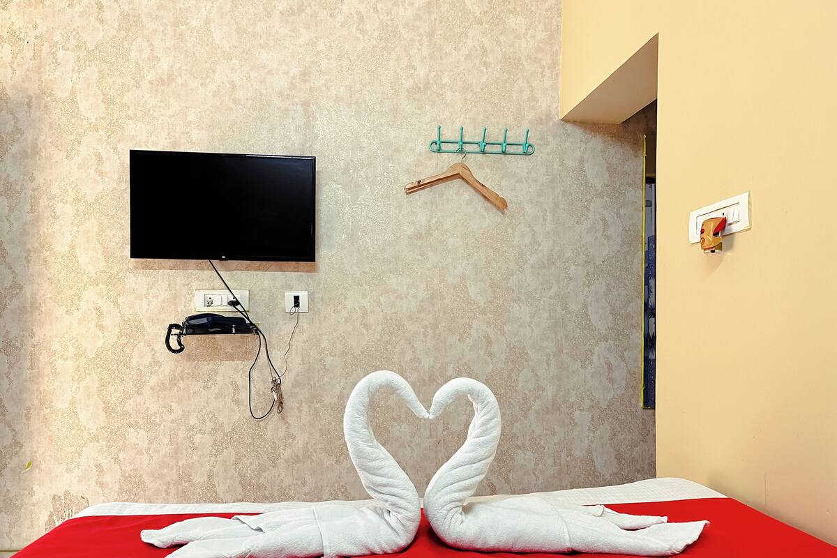 Quarto de hotel com cama, televisão fixada na parede, cabideiro e decoração com toalhas.