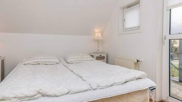Quarto com cama, mesa de cabeceira com abajur, janela com persianas e radiador.