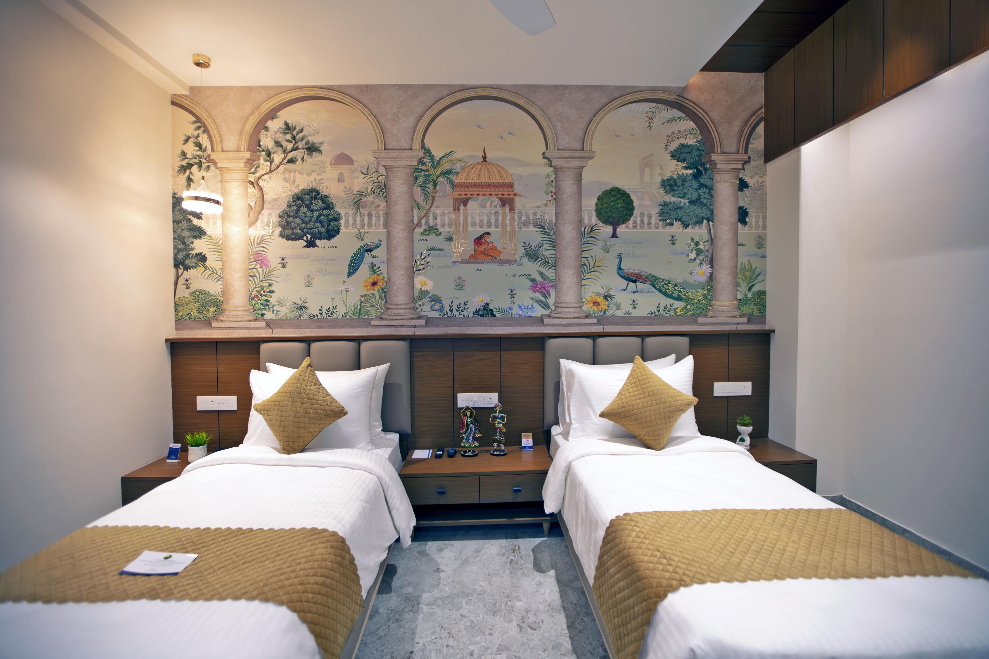 Quarto de hotel com duas camas, um mural na parede e uma mesa de cabeceira com abajur.
