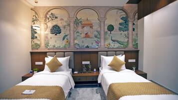 Quarto de hotel com duas camas, um mural na parede e uma mesa de cabeceira com abajur.