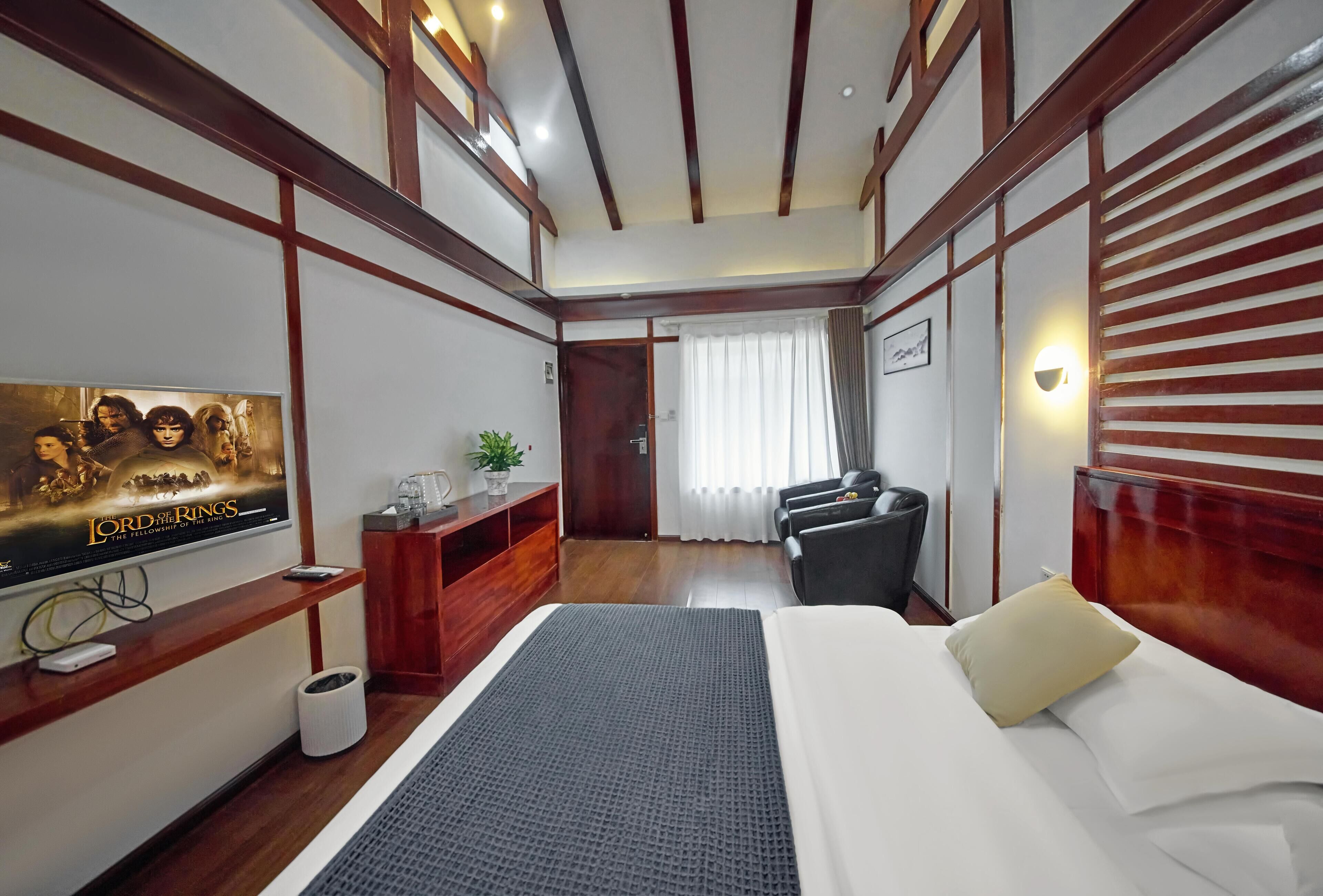 Quarto de hotel com uma cama grande, televisão na parede, escrivaninha com computador e janela com cortinas.