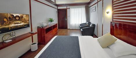 Quarto de hotel com uma cama grande, televisão na parede, escrivaninha com computador e janela com cortinas.