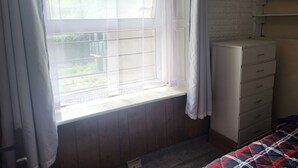 Um quarto com janela, paredes de madeira, cômoda branca e cama com colcha estampada.
