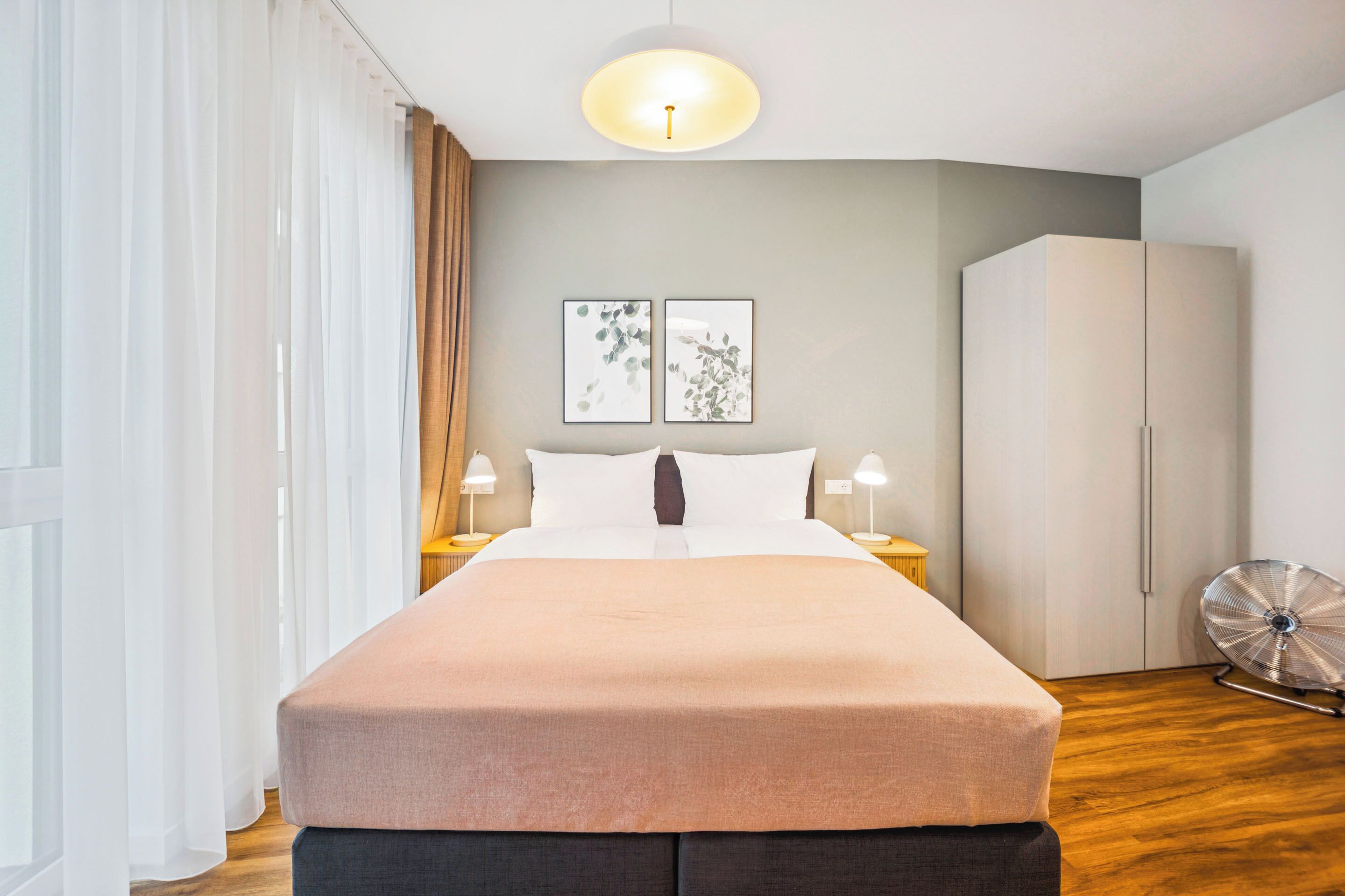 Quarto de hotel moderno com uma cama grande, abajures, uma luminária de teto e um guarda-roupa.