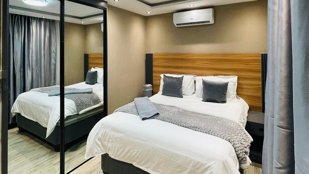 Quarto de hotel moderno com uma cama grande, um espelho, um aparelho de ar condicionado e uma luminária no teto.