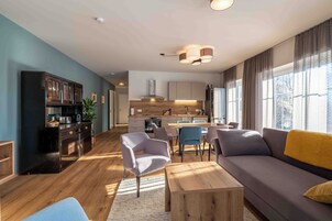 Uma sala de estar moderna com sofá, cadeiras, mesa de centro e cozinha ao fundo.