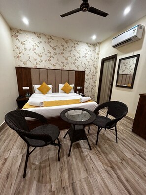 Quarto de hotel com cama, duas cadeiras, mesa, ventilador de teto, ar condicionado e espelho na parede.