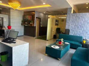 Um hall moderno de hotel com uma mesa de recepção, uma mesa de centro de vidro, sofás verde-água e um lustre.