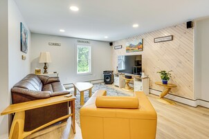 Uma sala de estar moderna com um sofá de couro marrom, um banquinho amarelo, uma mesa de centro de madeira e uma televisão.