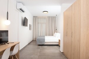 Quarto de hotel moderno com cama, escrivaninha com computador, televisão e guarda-roupa.