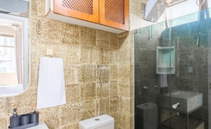 Casa de banho com azulejos de granito, um armário de madeira, cabine de duche em vidro e sanita.