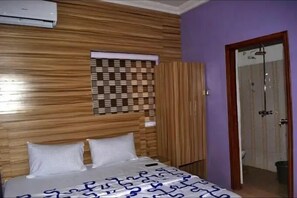 Quarto com cabeceira de madeira, cama com roupa de cama branca e janela com persiana xadrez.