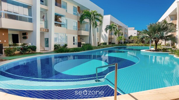 Um hotel moderno com piscina, várias varandas e palmeiras.