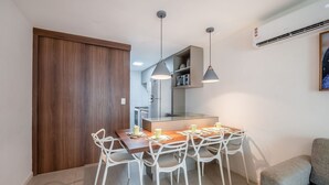 Cozinha moderna com área de refeições, cadeiras brancas, luminárias pendentes e sofá cinza.
