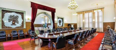 Uma sala de conferências com uma mesa comprida, várias cadeiras e um tapete vermelho.