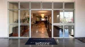 Entrada de um hotel com fachada de vidro, balcão de recepção e uma placa com a inscrição "RESIDENCIAL".