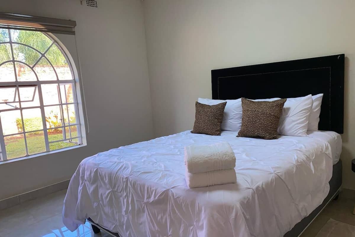 Cama bem arrumada com lençóis brancos, toalha dobrada, cabeceira preta e duas almofadas com estampa de leopardo.