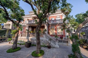 Edifício tradicional com uma escadaria central, rodeado por plantas e árvores em vasos.