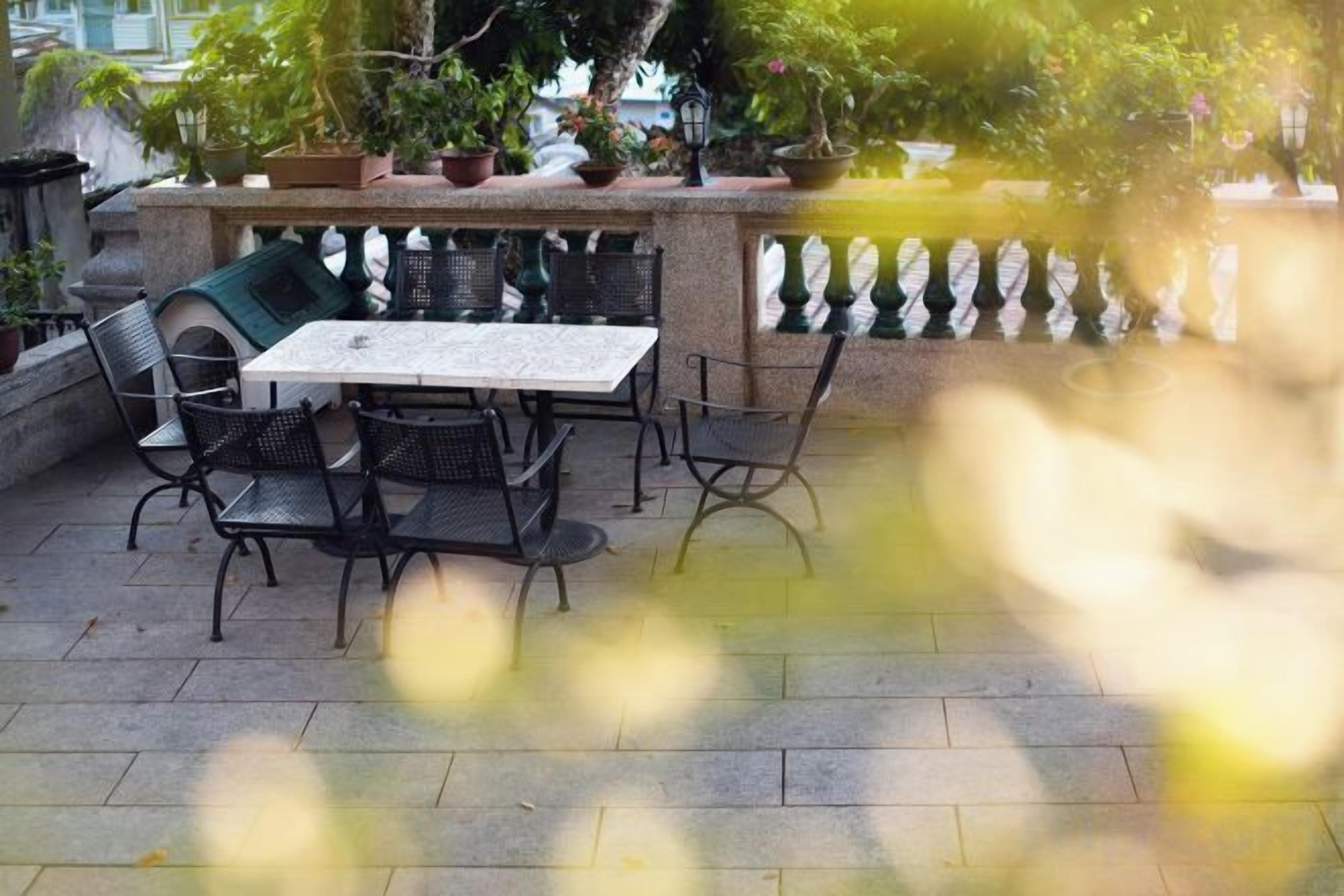 Um pátio externo com mesa e cadeiras, rodeado por plantas em vasos e um cercado decorativo.