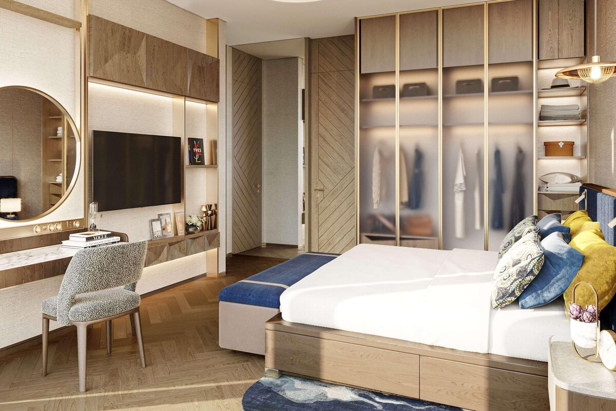 Quarto moderno com uma cama grande, uma escrivaninha com cadeira, um guarda-roupa e uma televisão.