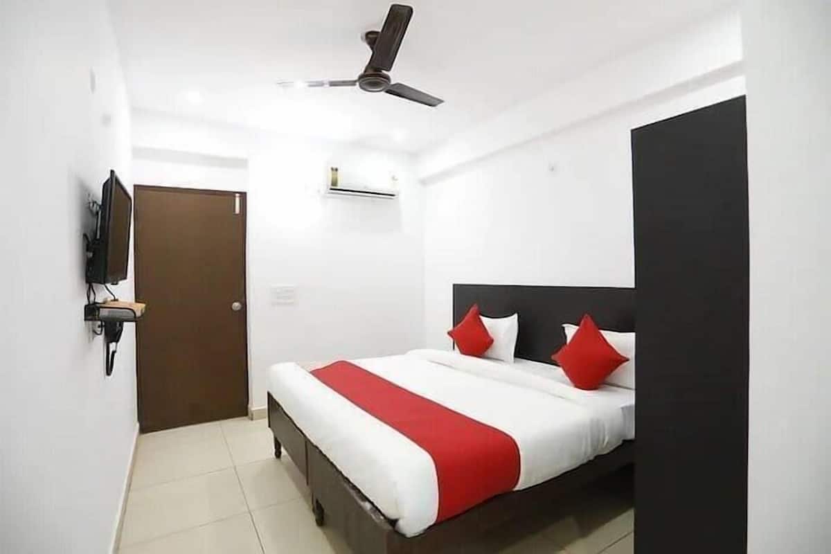 Quarto de hotel com uma cama, um ventilador de teto, uma televisão fixada na parede e uma porta.