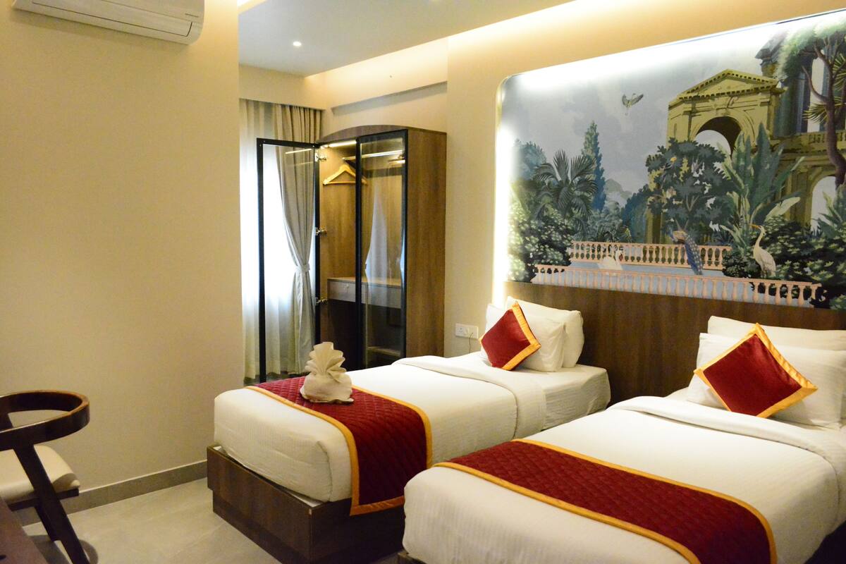 Quarto de hotel com duas camas, um guarda-roupa, um espelho e um quadro com uma paisagem tropical.
