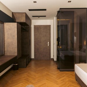 Quarto moderno com piso de madeira em padrão herringbone, uma cama, um guarda-roupa e uma porta de vidro que dá para outro cômodo.