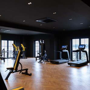 Academia moderna com diversos equipamentos de ginástica, amplas janelas e piso de madeira.
