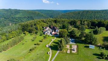 Vista aérea de uma propriedade rural com um conjunto de casas rodeadas por vegetação exuberante e colinas.