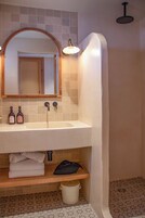 Casa de banho com lavatório, espelho, porta-toalhas e chuveiro.