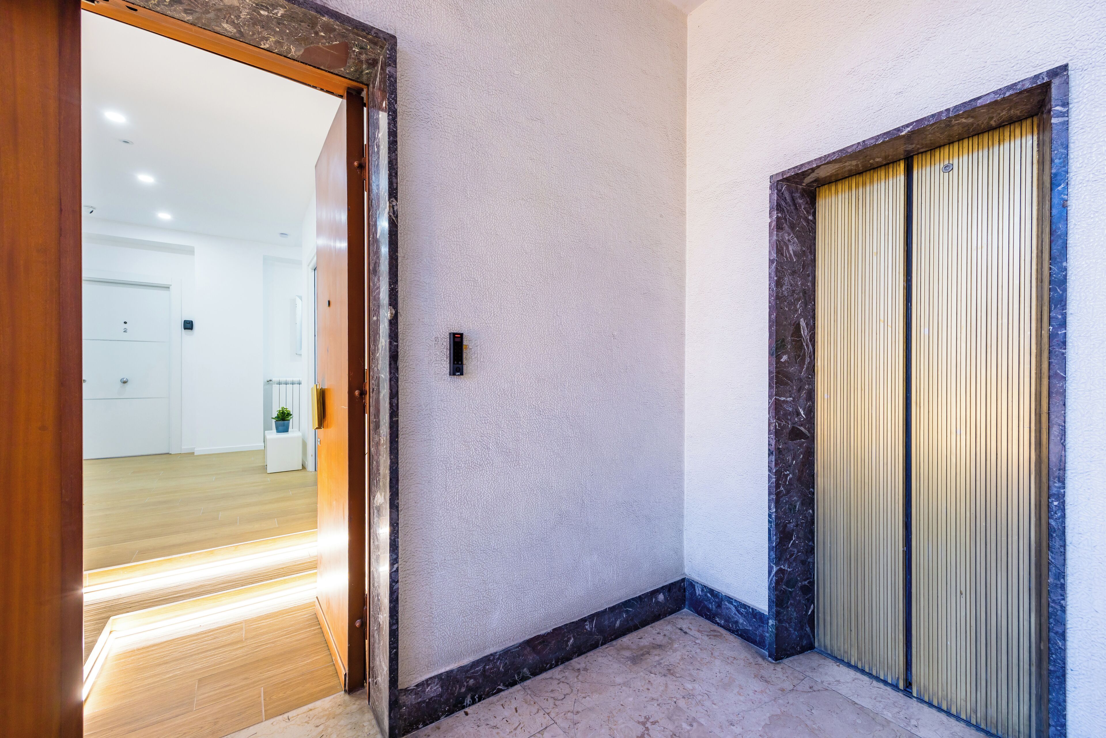 Um corredor com uma porta de madeira, um revestimento de mármore e uma porta amarela fechada.