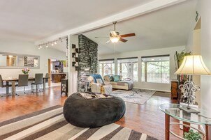 Uma sala de estar espaçosa com parede de destaque em pedra, ventilador de teto, área de jantar com mesa e cadeiras, e uma grande janela que oferece luz natural.