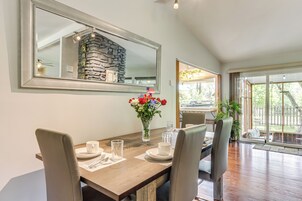 Uma sala de jantar com uma mesa de madeira, quatro cadeiras, um vaso com flores e um espelho grande na parede.