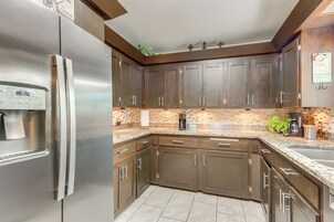 Cozinha com armários de madeira escura, geladeira de aço inoxidável e painel de azulejos.