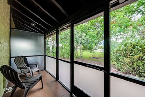 Espaço coberto ao ar livre com banco e janelas amplas com vista para um jardim.