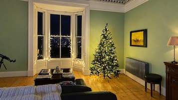 Quarto com uma grande janela em arco, uma árvore de Natal, um quadro na parede e uma luminária.