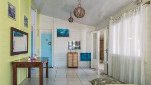 Um quarto com uma mesa de madeira, um banco, um armário de vime e uma porta que dá para outro cômodo.
