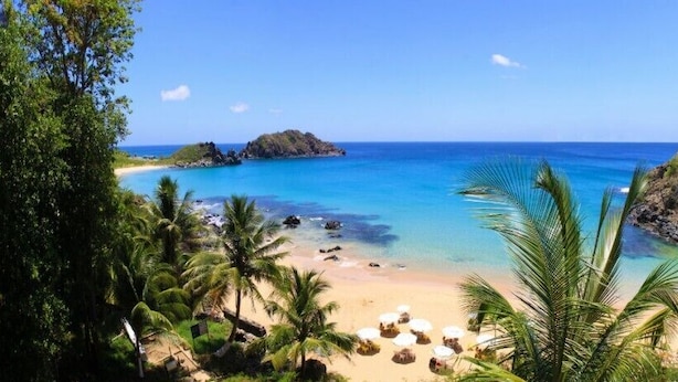 Uma praia com águas turquesa cristalinas, areal arenoso e vegetação exuberante.