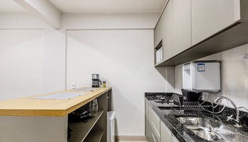 Uma cozinha compacta com cafeteira, micro-ondas e lava-louças embutida.