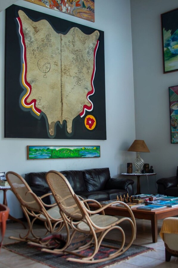 Uma sala de estar com um grande painel decorativo, um sofá, duas poltronas de balanço, uma mesa de centro e um abajur.