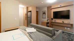 Quarto de hotel com cama, sofá, escrivaninha, televisão e frigorífico.