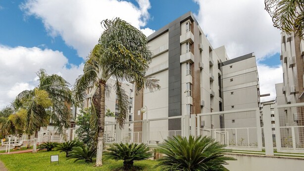 Um edifício moderno com vários andares, grandes janelas e um jardim circundante com palmeiras.